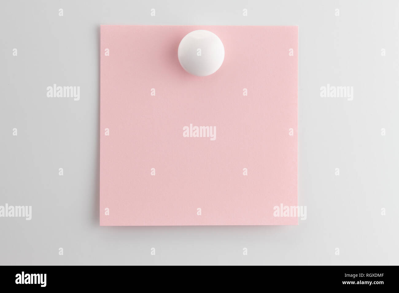 Square blank sheet of pink paper pinned with a white button magnet on ...