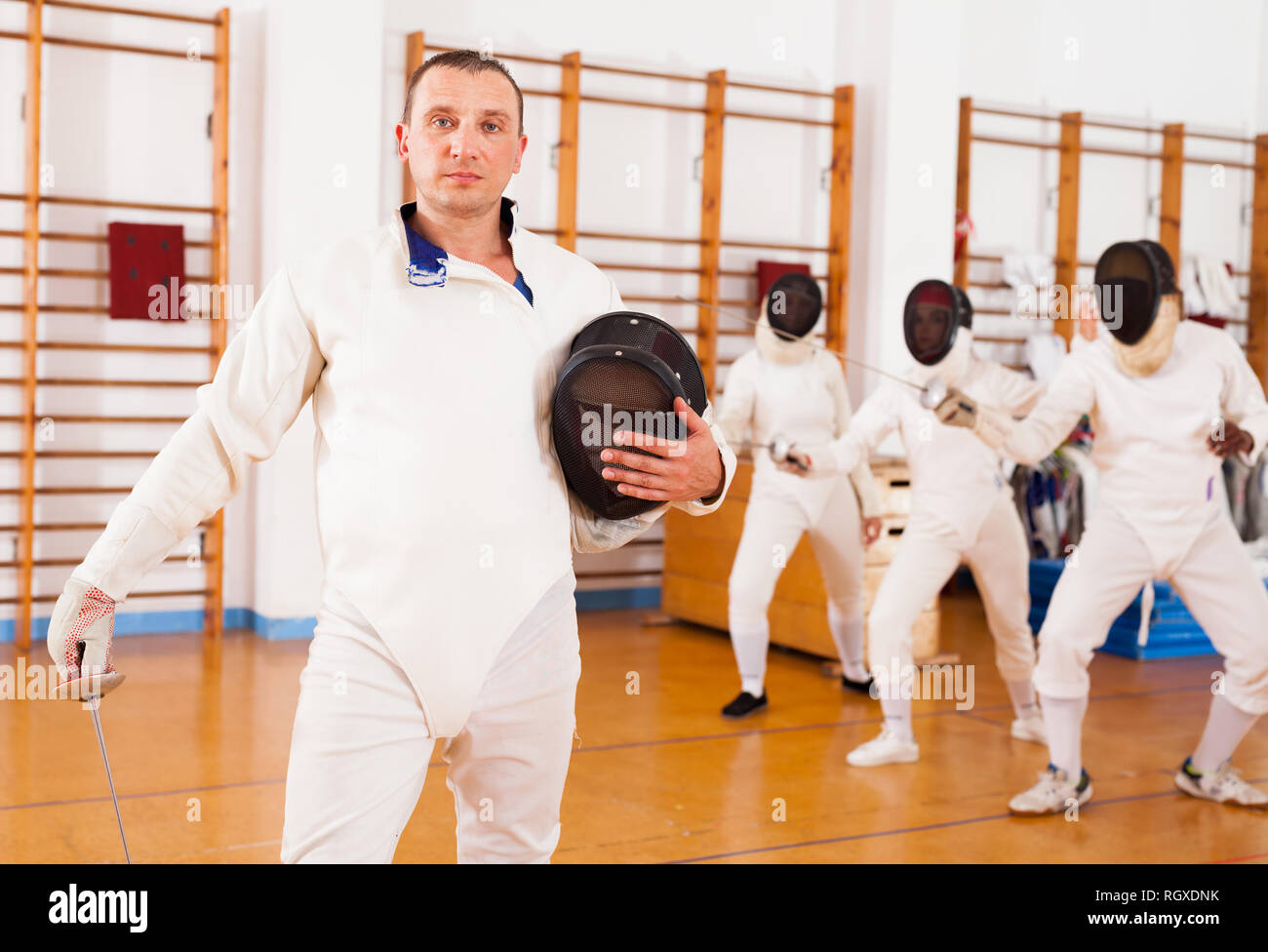 Sporty young man fencer in uniform standing with mask and foil at ...