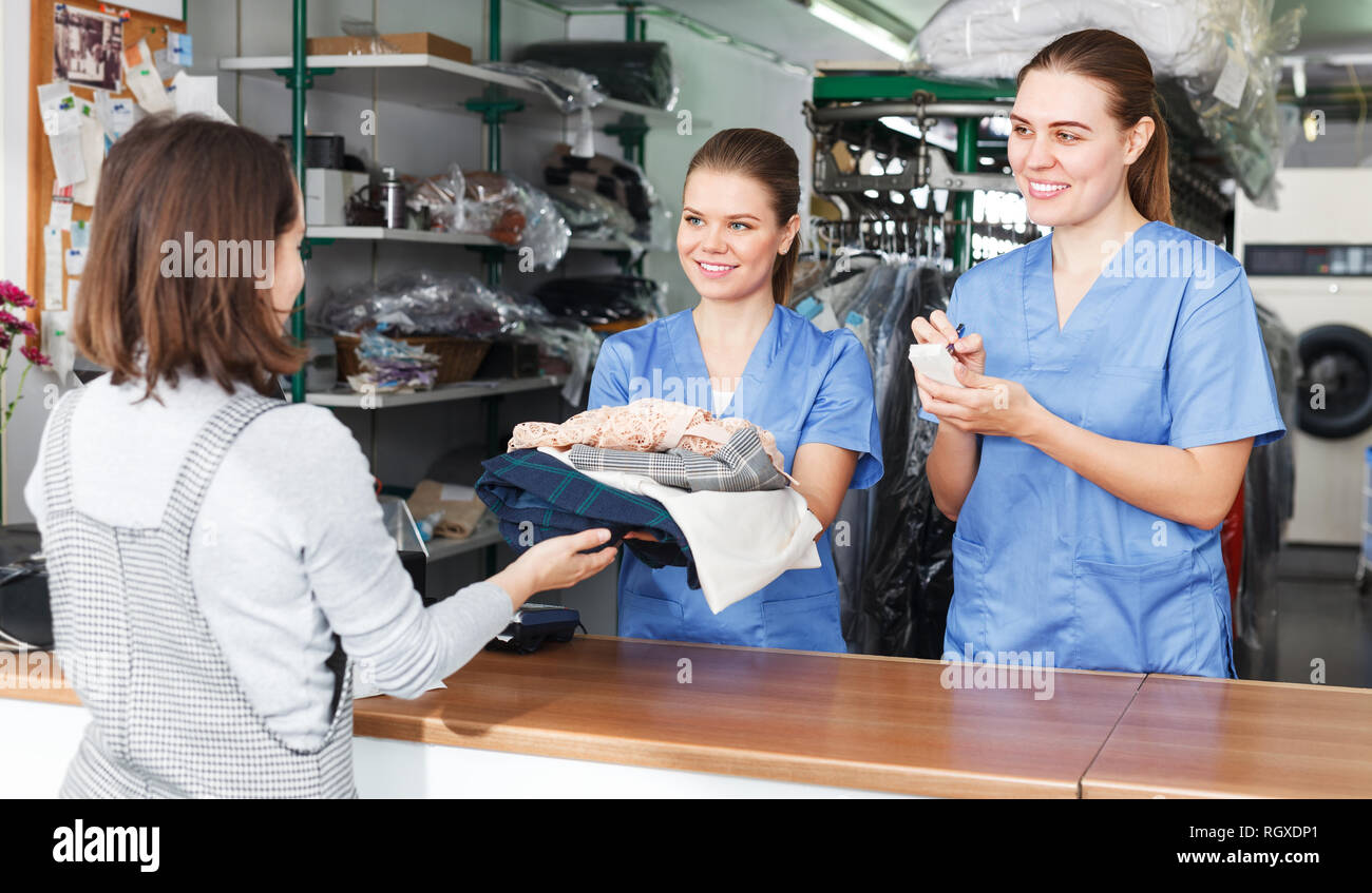 Young polite woman worker of laundry giving clothes after dry cleaning ...