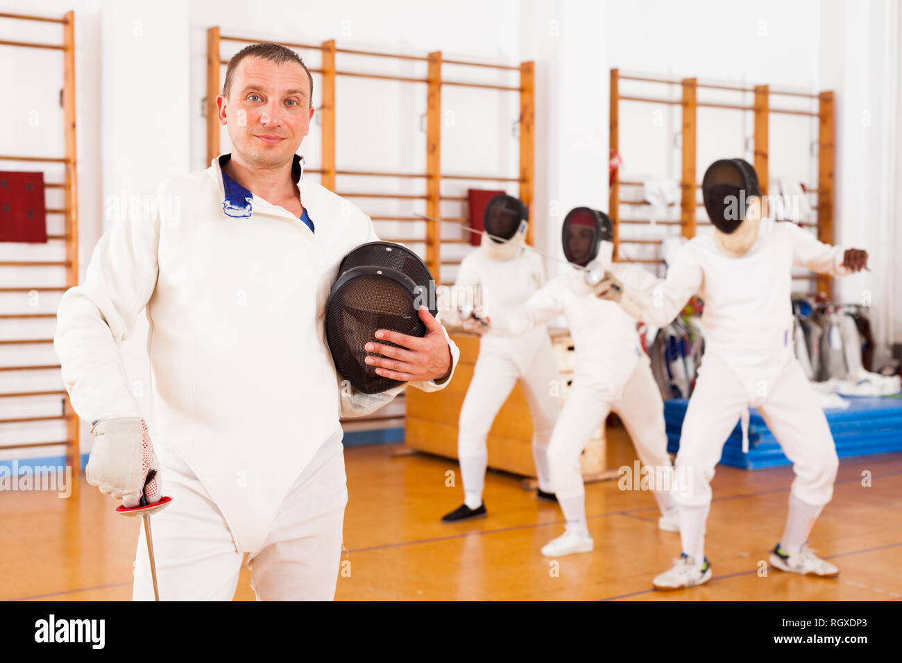 Young man fencer in uniform and mask standing with foil at fencing ...