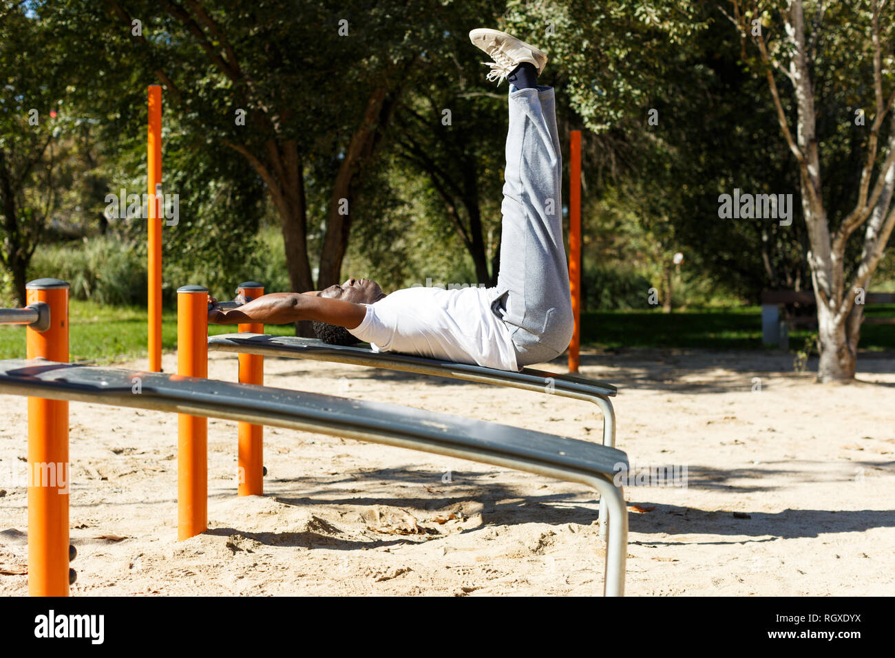 Active young male doing leg raises at sports ground in park outdoor ...