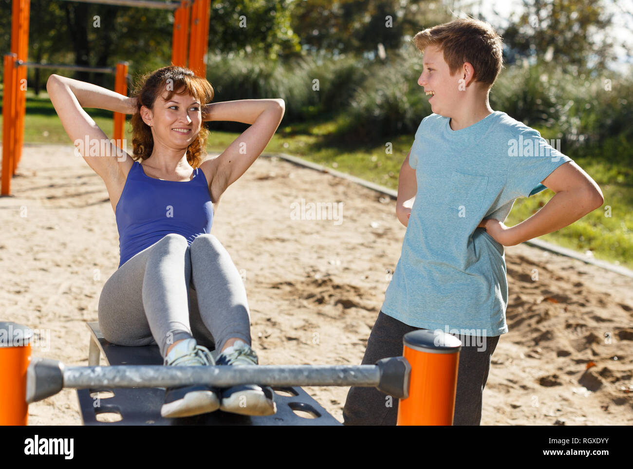 Smiling athletic woman doing push-ups while her son standing nearby and ...
