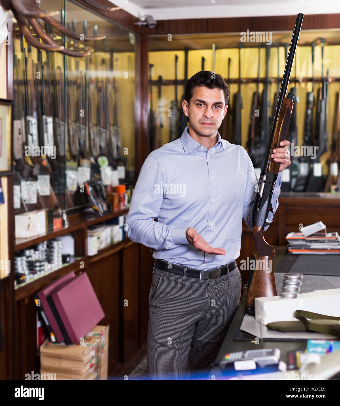 Portrait of positive salesman in gun store showing shotgun Stock Photo ...