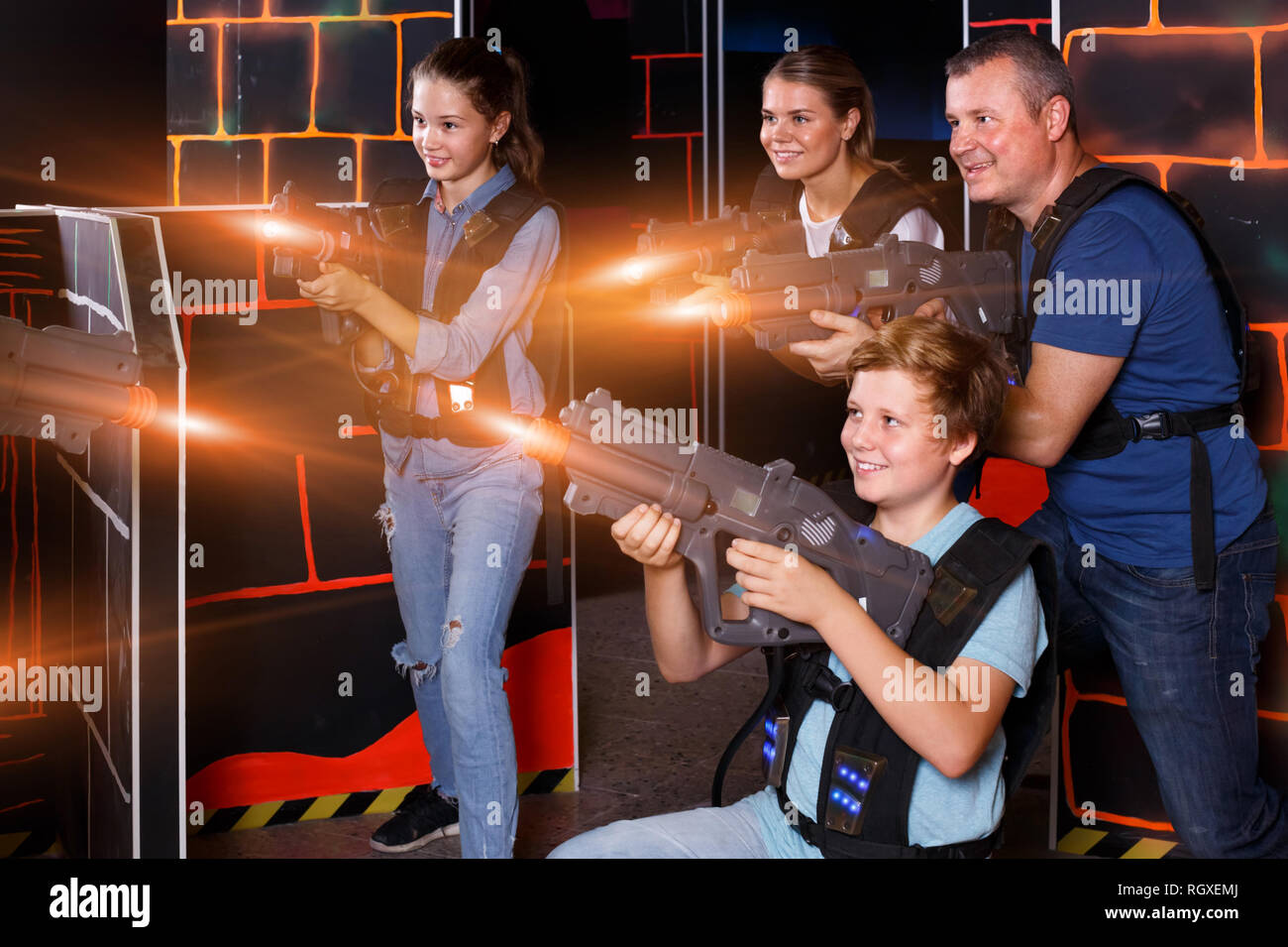 joyous young parents and children with laser pistols playing laser tag ...