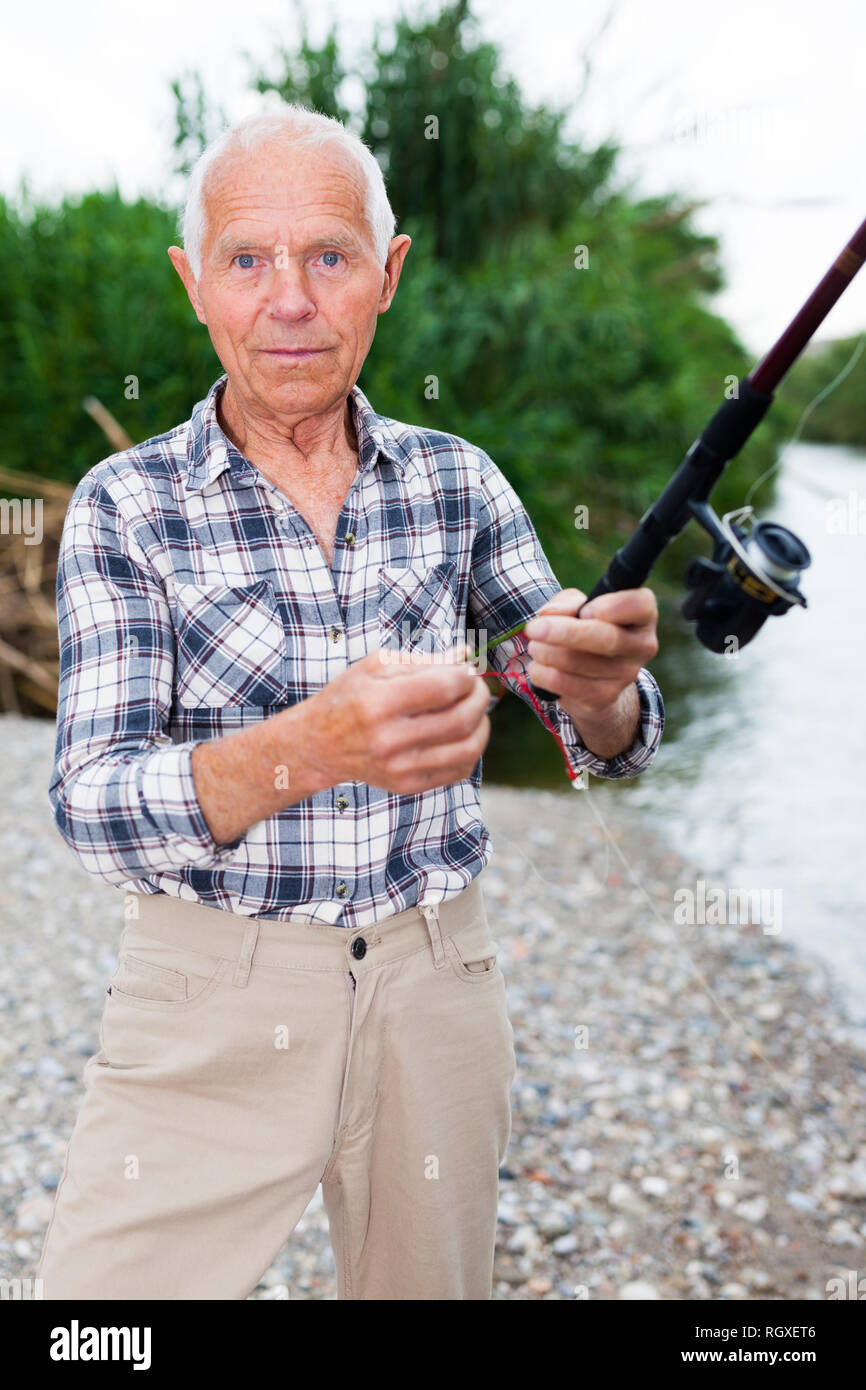 Positive adult man with rod relaxing and enjoying fishing by lakeside ...