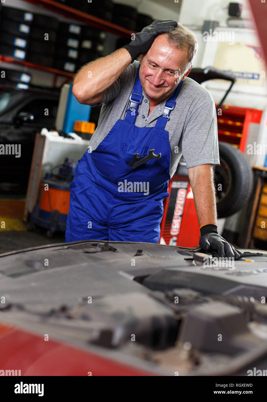 Puzzled male mechanic inspecting broken car and determining scope of ...