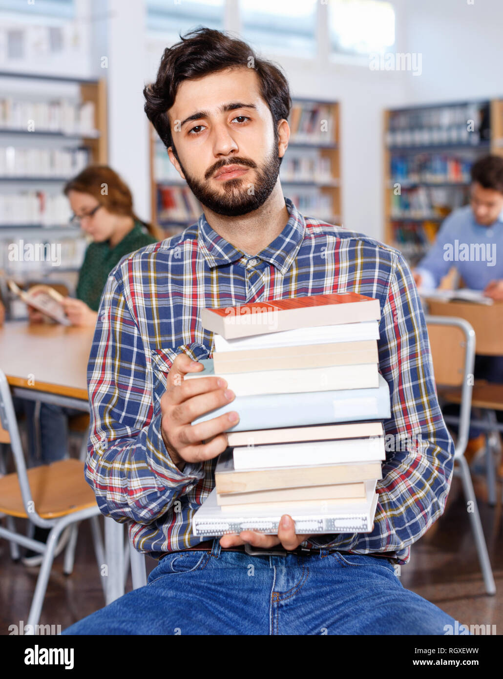Tired melancholy angry man sitting with pile of books in university ...