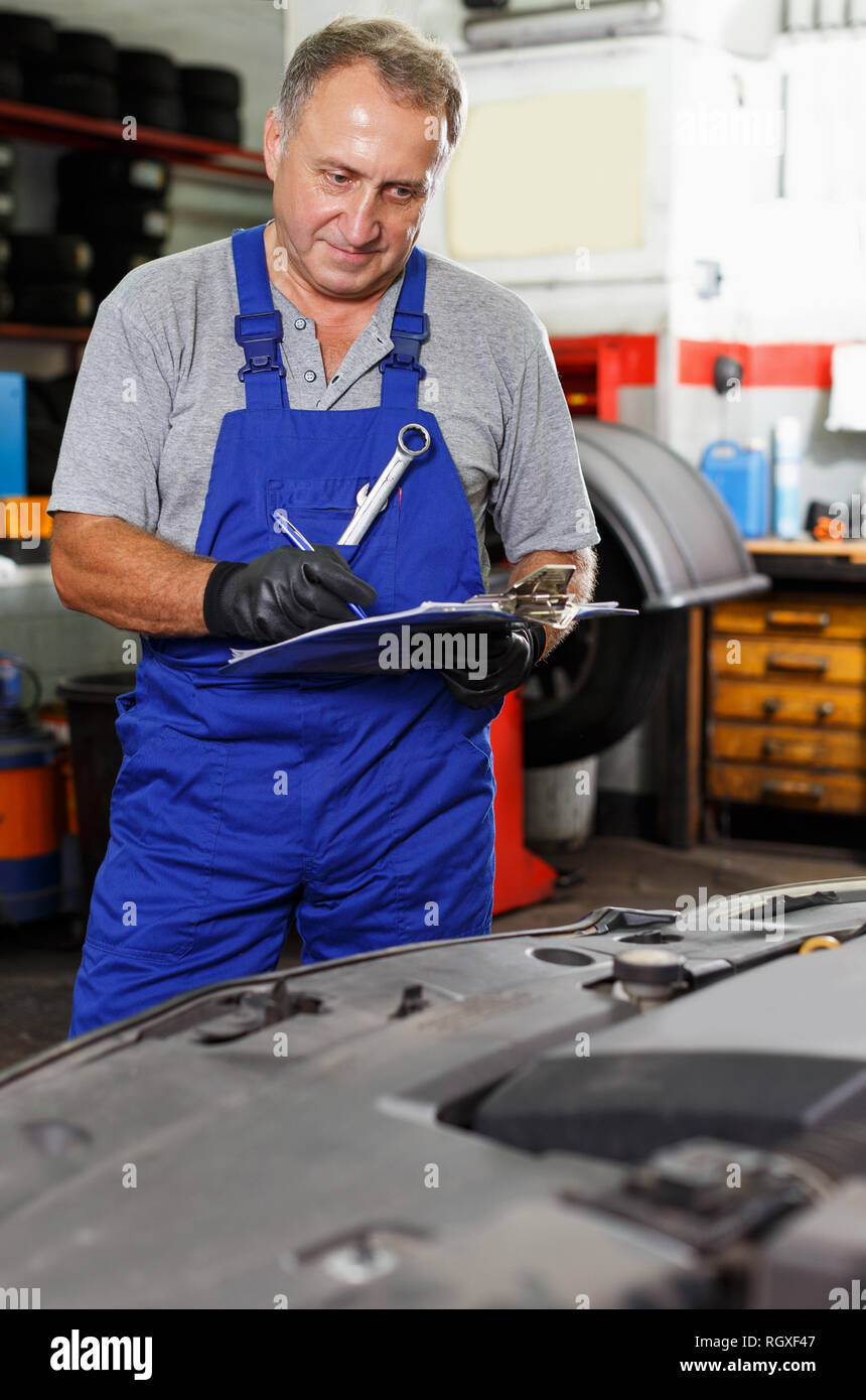 Professional serious auto mechanic recording list of works on car ...