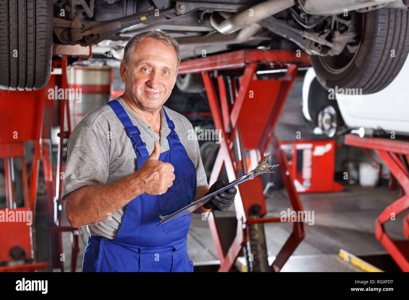 Confident male car mechanic in a workshop writing job sheet for repairs ...