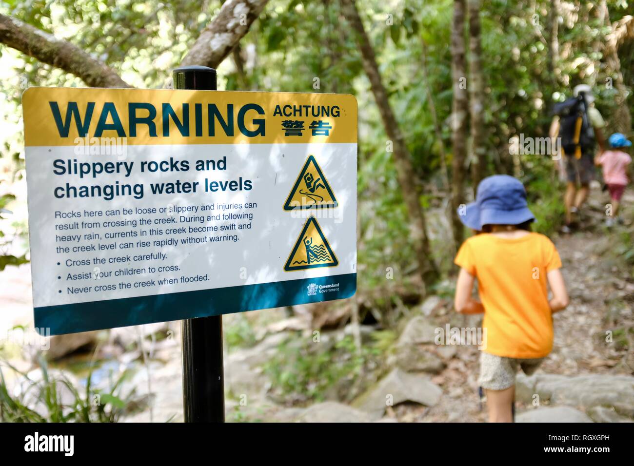 Children and a father walk past a warning slippery rocks and changing ...