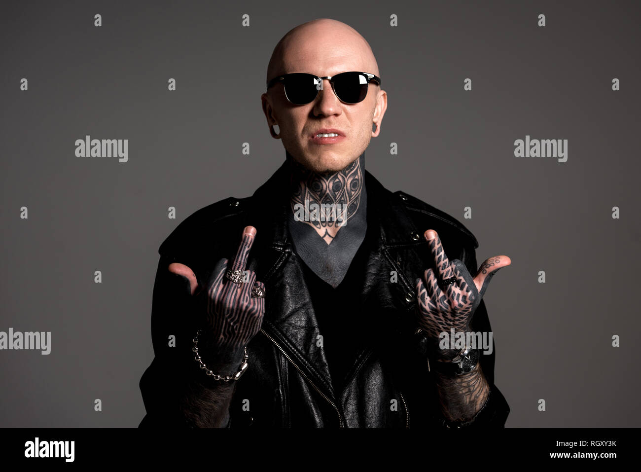 aggressive tattooed man in leather jacket and sunglasses showing middle ...