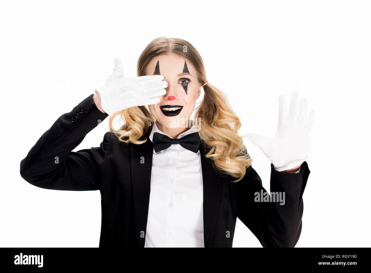 cheerful female clown standing in suit and covering eye with hand in ...