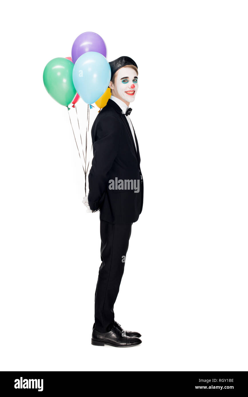 cheerful clown in suit and black beret holding helium balloons behind ...