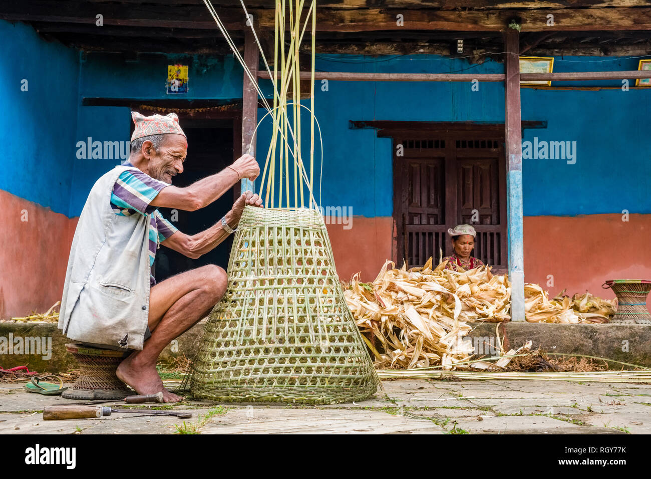 Local man braiding a basket, his wife harvesting corn behind him at his ...