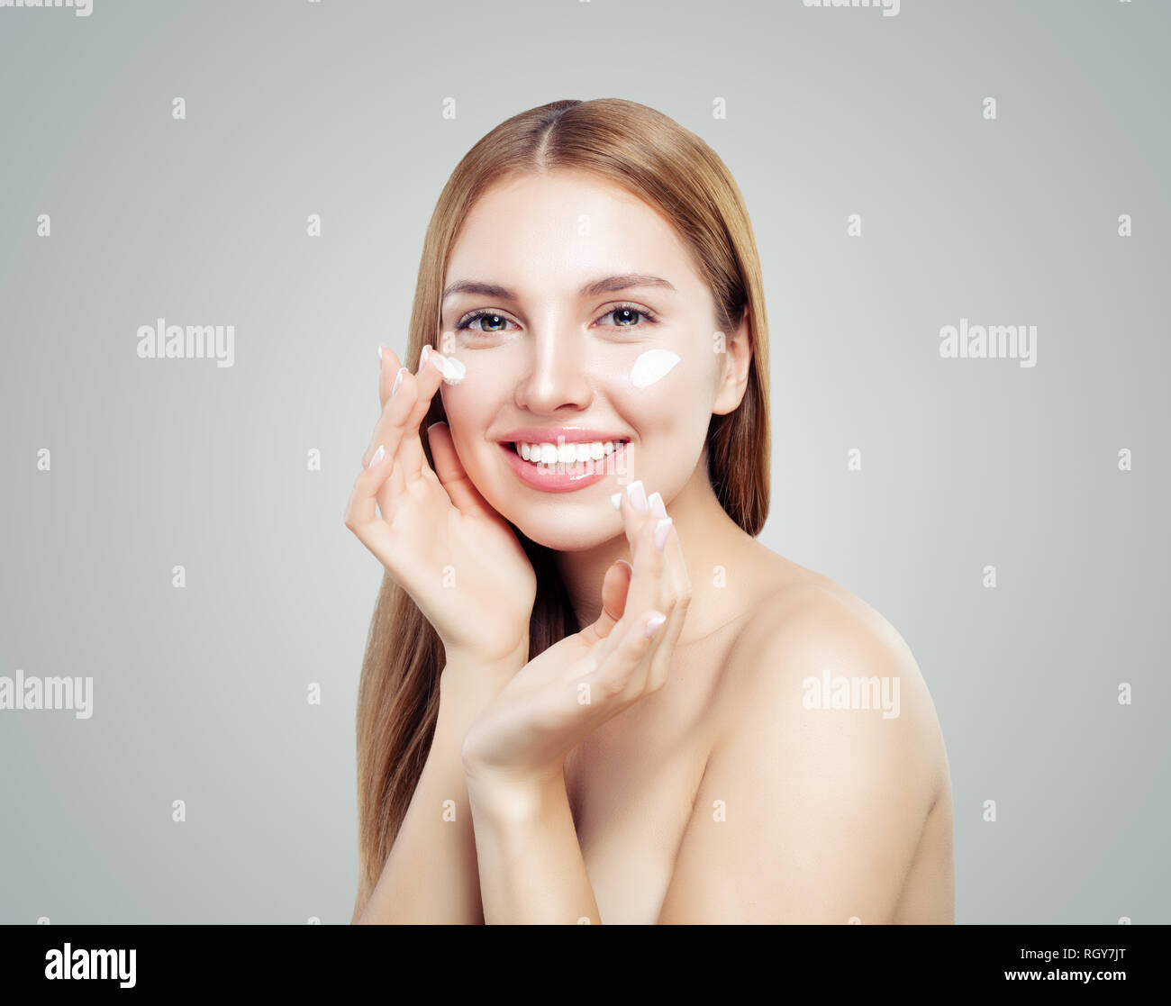 Beautiful model girl applying cosmetic cream treatment on her face on white. Healthy woman ...