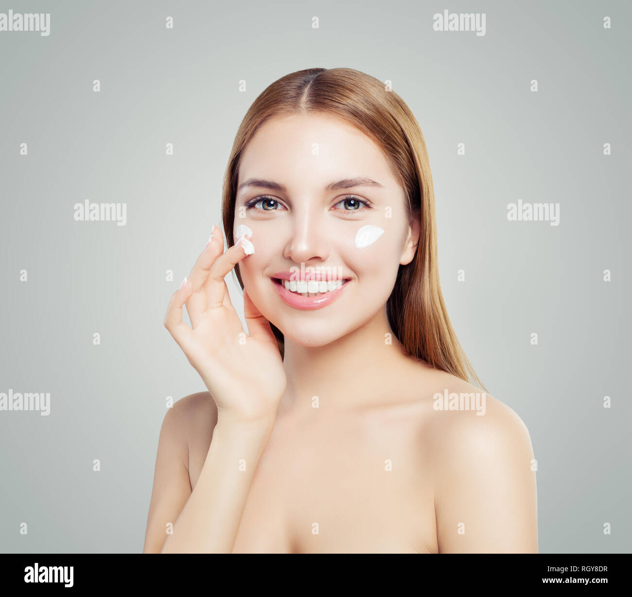 Cheerful female model applying anti-aging cream on her face. Skin care ...