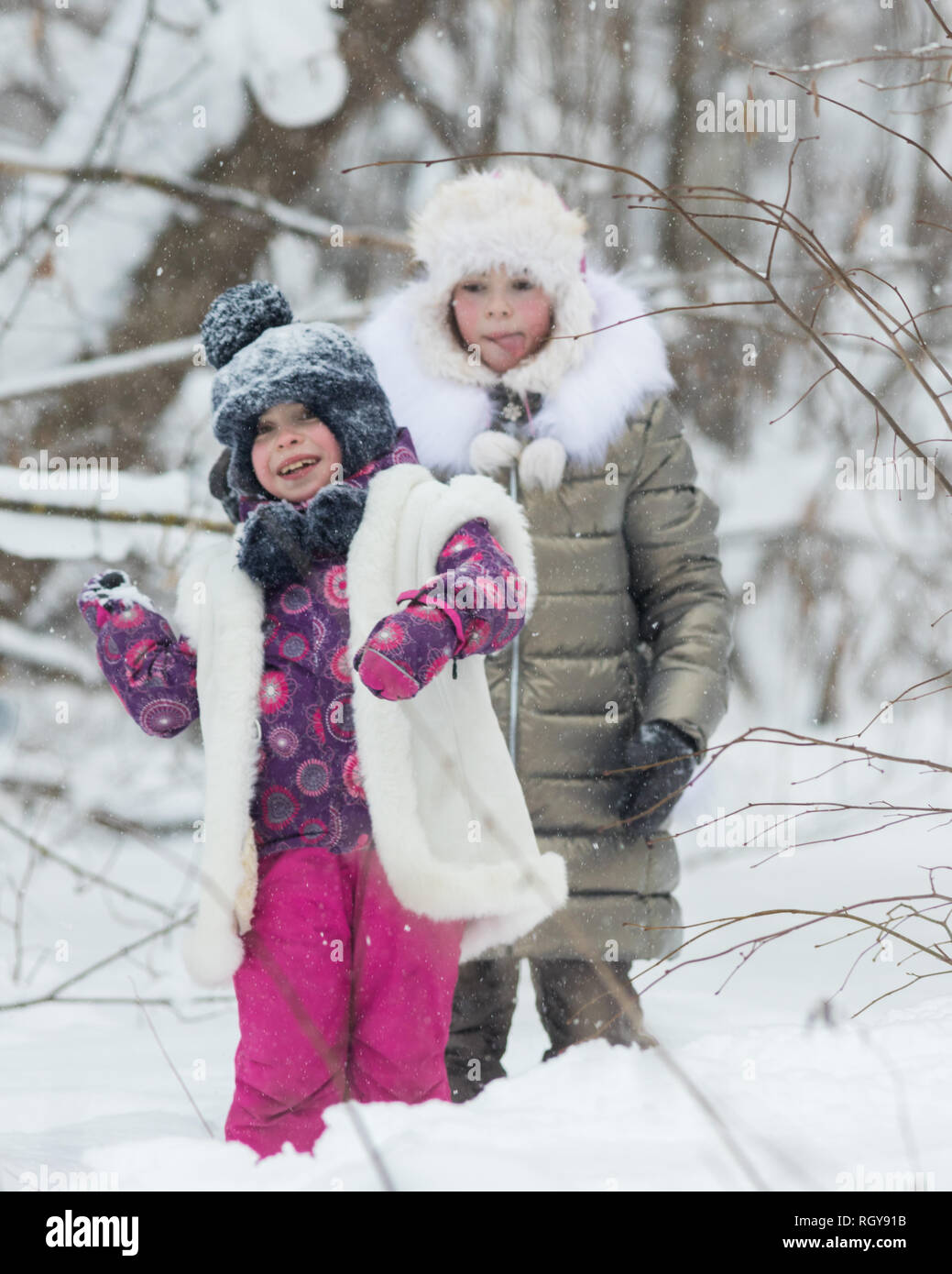Winter forest. Two little girls playing snowballs. Smiling. Mid shot ...