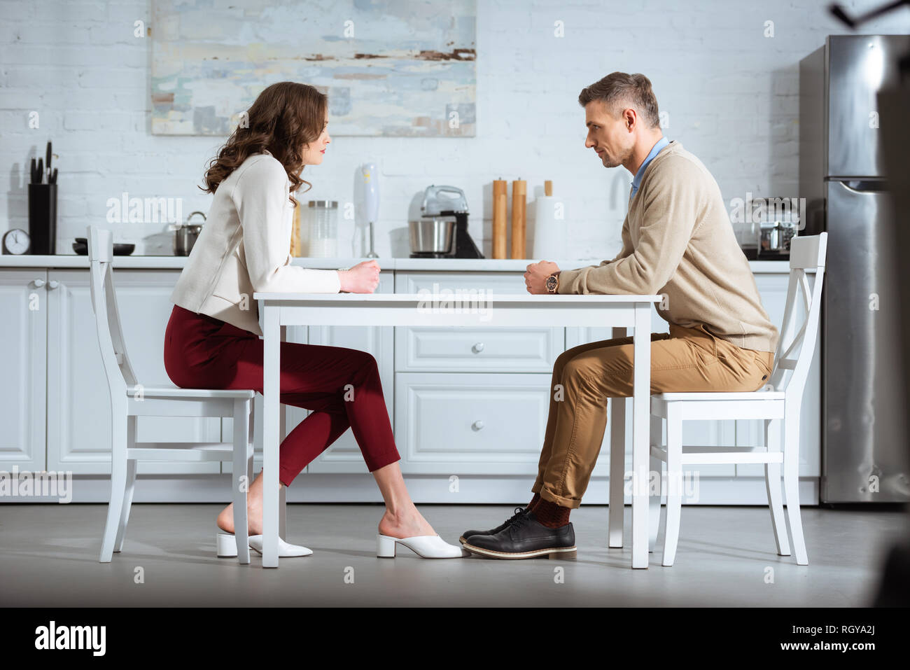 dissatisfied couple sitting with clenched fists at table in kitchen ...