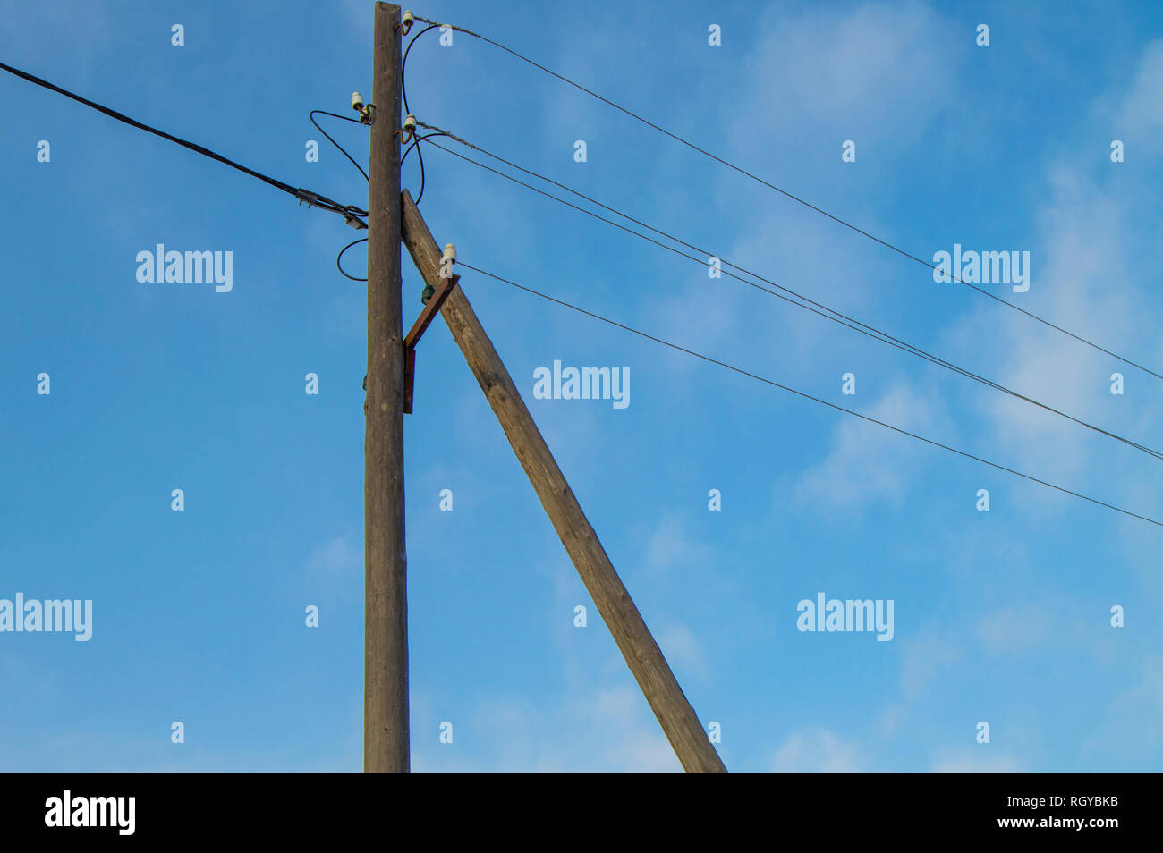 Wooden old 0.4 kV power line support with wires and insulators on blue ...