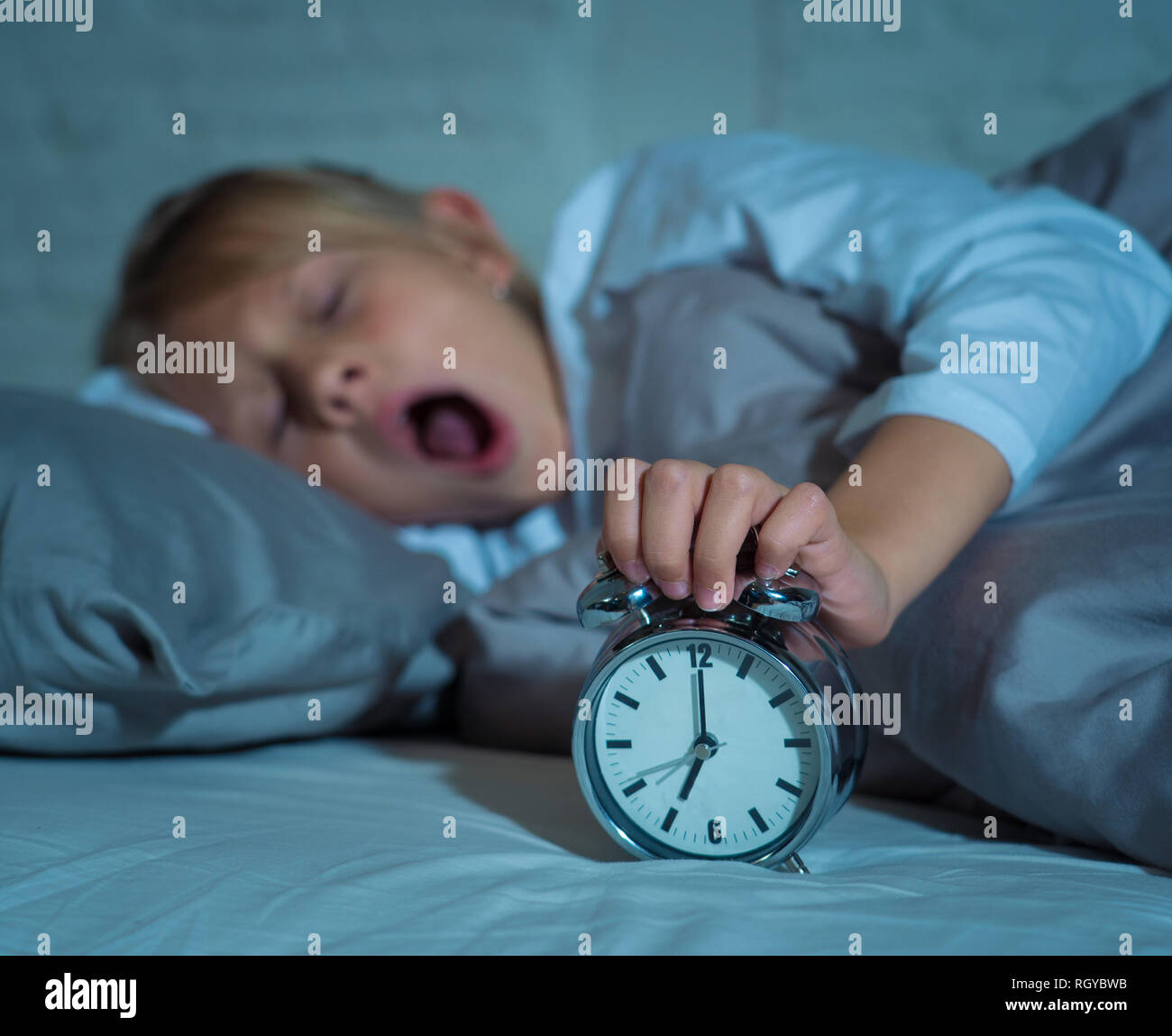 Sweet sleepless little girl lying sad in bed looking at alarm clock ...