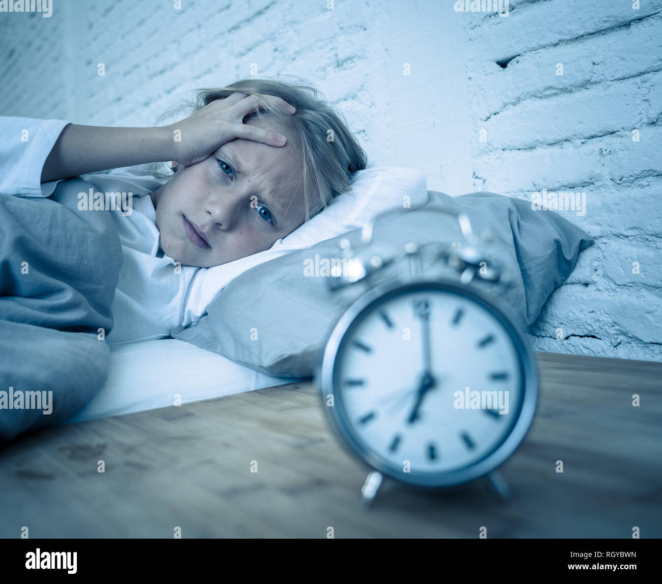 Sweet sleepless little girl lying sad in bed looking at alarm clock ...