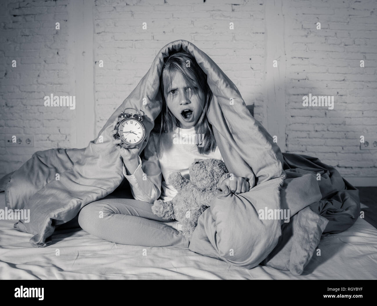 Cute sleepless little girl sitting on bed looking sad and tired having ...