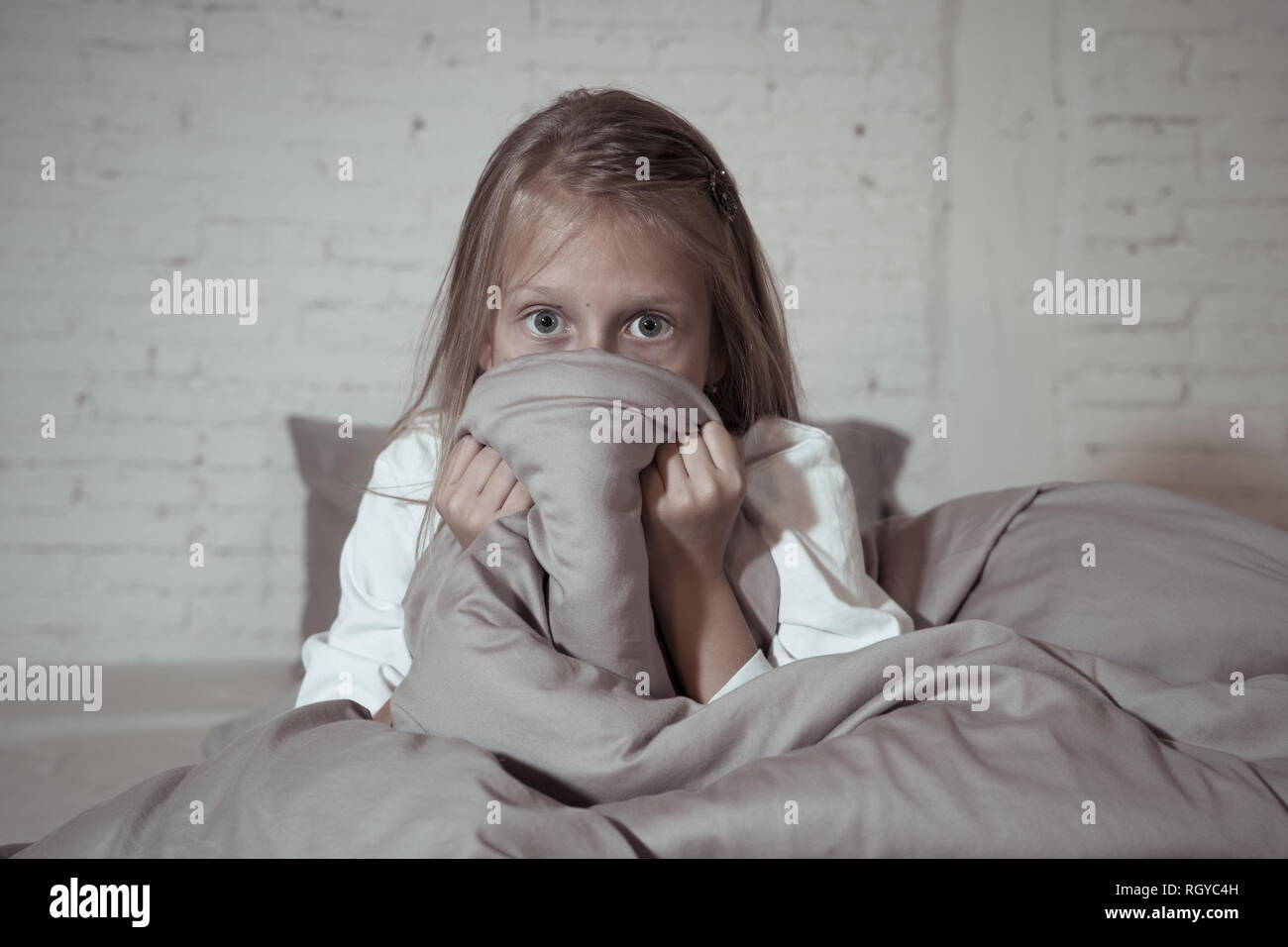 Scared little girl staying sleepless hiding behind the duvet looking ...