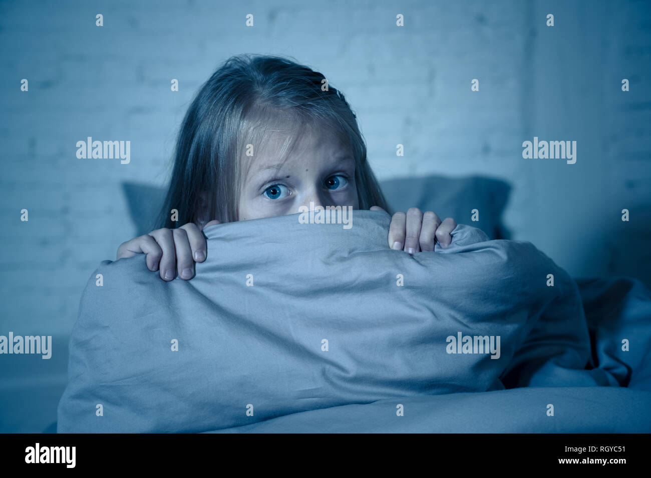 Scared little girl staying sleepless hiding behind the duvet looking ...