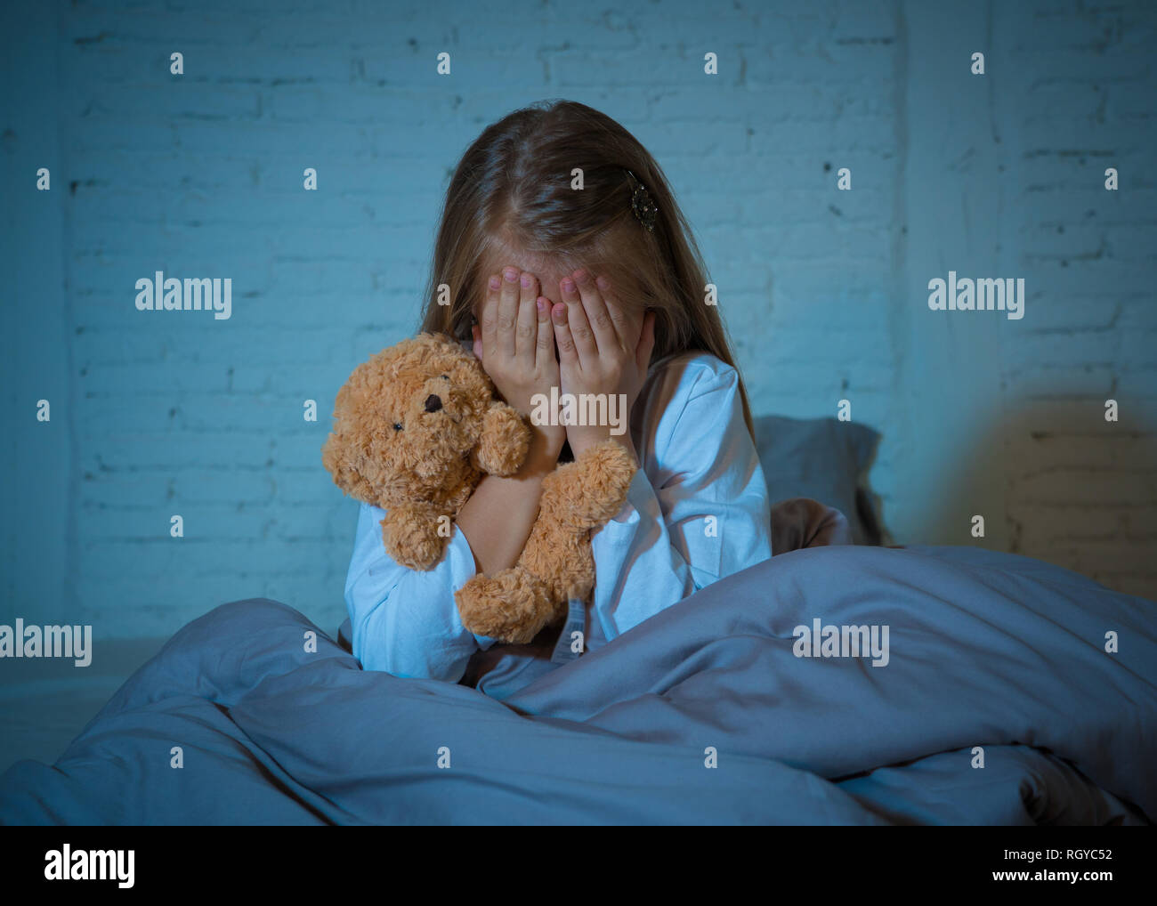 Scared little girl sitting in bed covering her face with hands holding ...