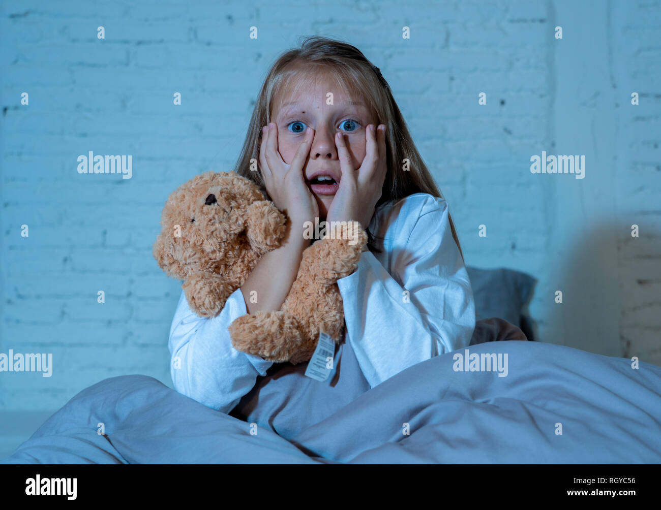 Scared little girl sitting in bed covering her face with hands holding ...