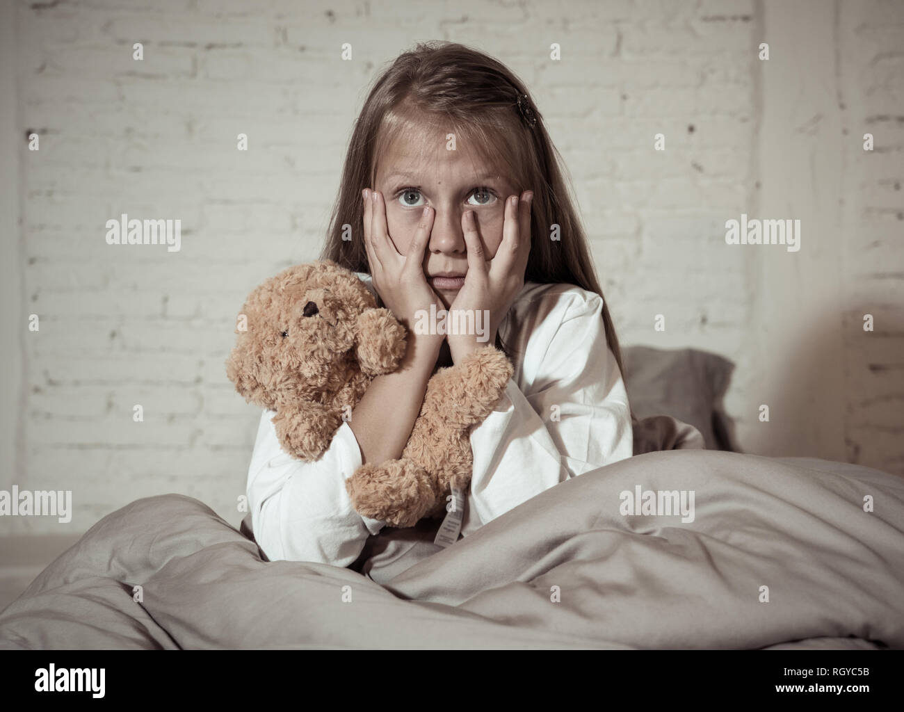 Scared little girl sitting in bed covering her face with hands holding ...
