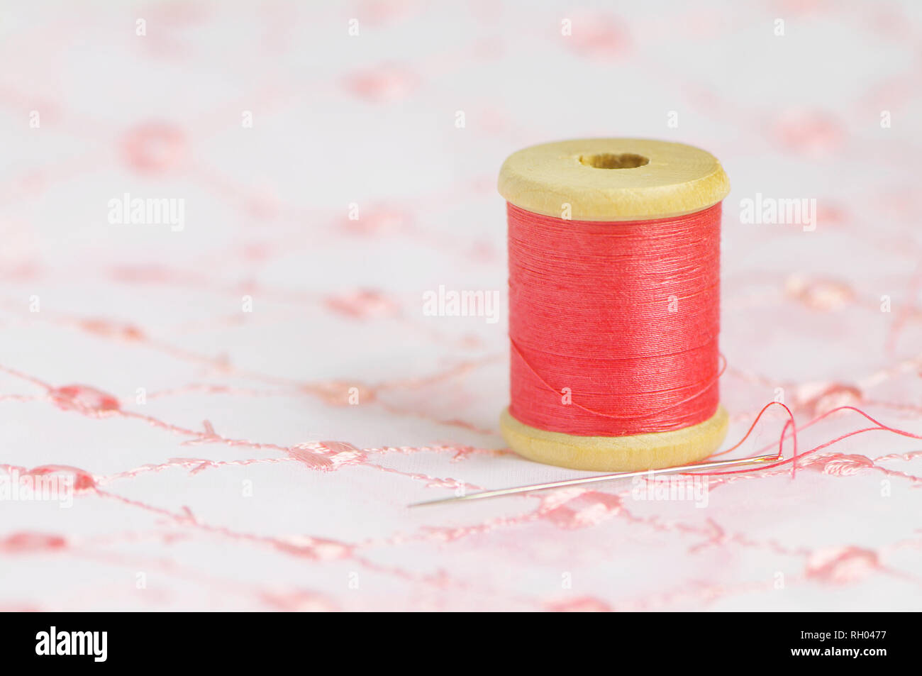 Coral coloured thread on a wooden spool and needle on a detailed ...
