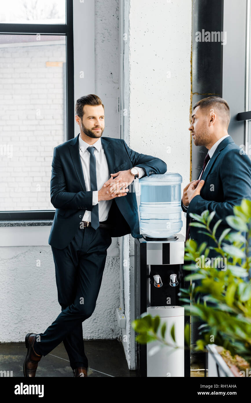 businessman standing with crossed legs and talking with coworker in ...