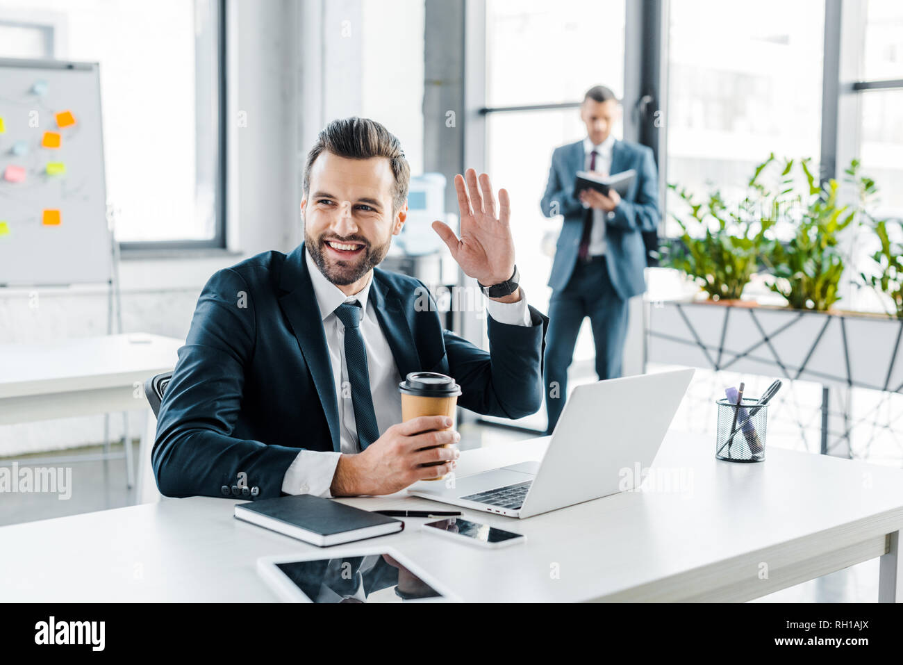 selective focus of cheerful man in formal wear waving hand with ...