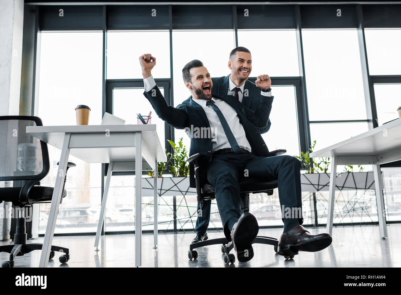 happy businessman riding on chair near coworker in modern office Stock ...