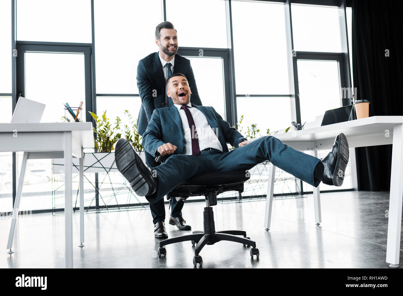 happy businessman pushing chair with cheerful coworker in modern office ...