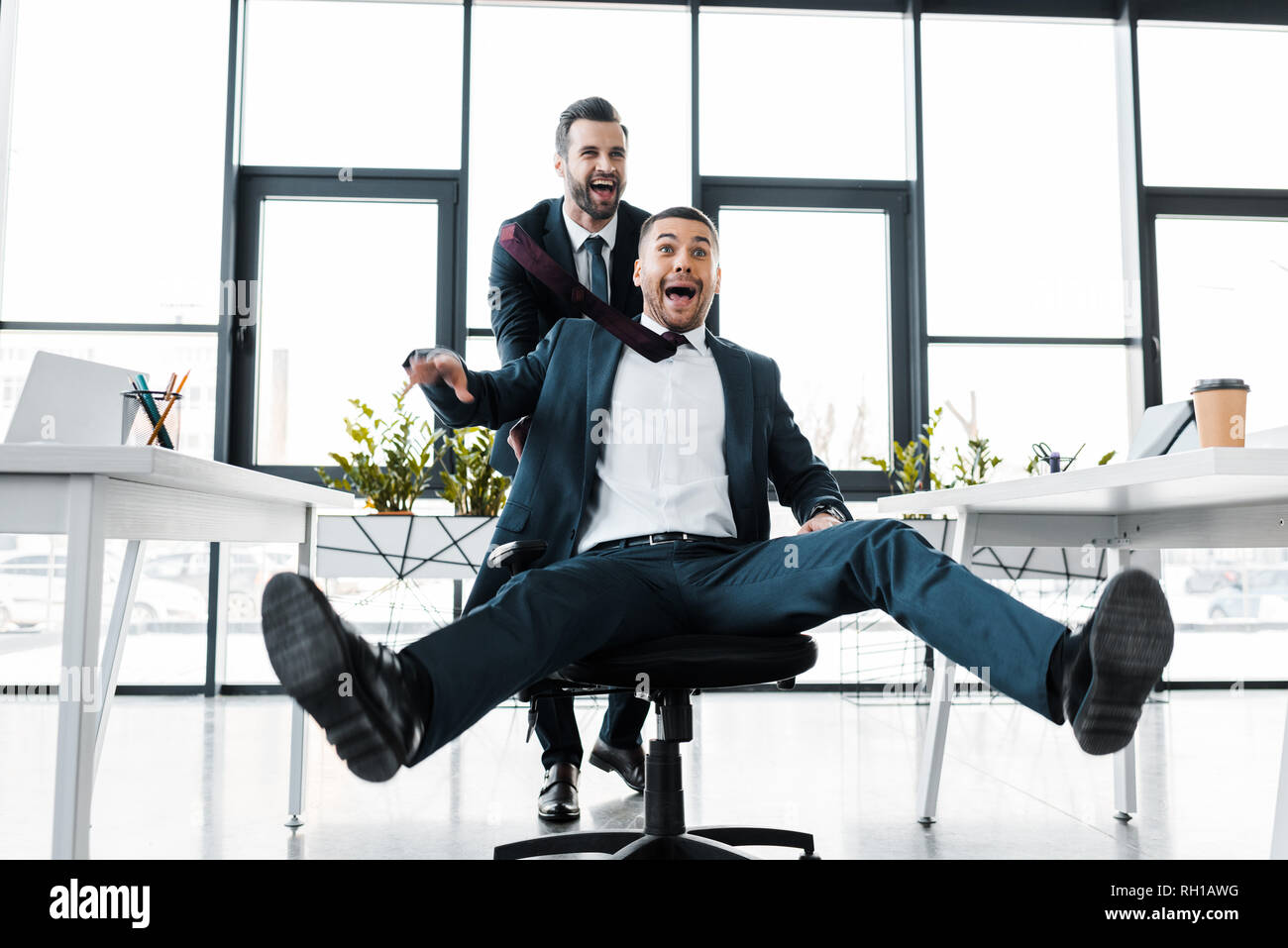 happy businessman pushing chair with excited coworker in modern office ...