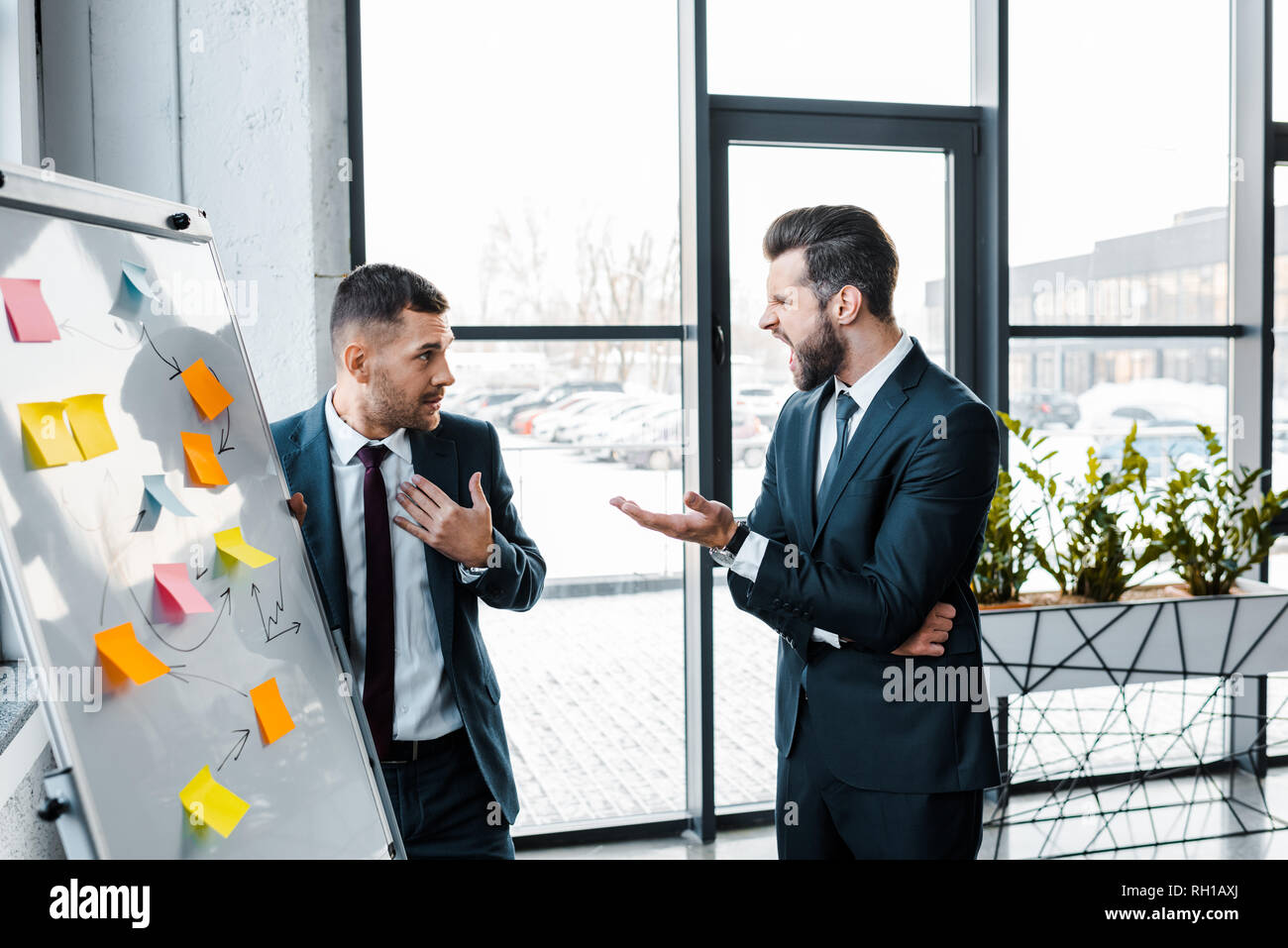 angry businessmen screaming at coworker near white board in modern ...