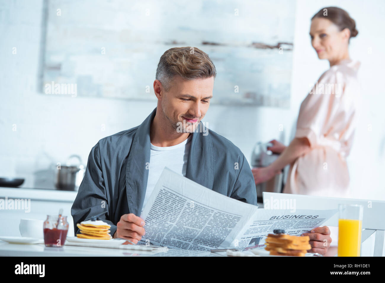 man reading newspaper during breakfast while woman cooking on ...