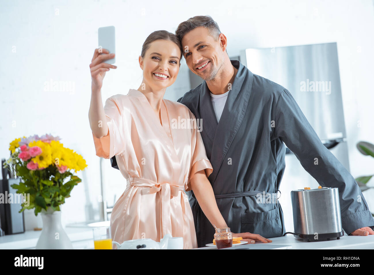 beautiful happy couple in robes taking selfie on smartphone during ...