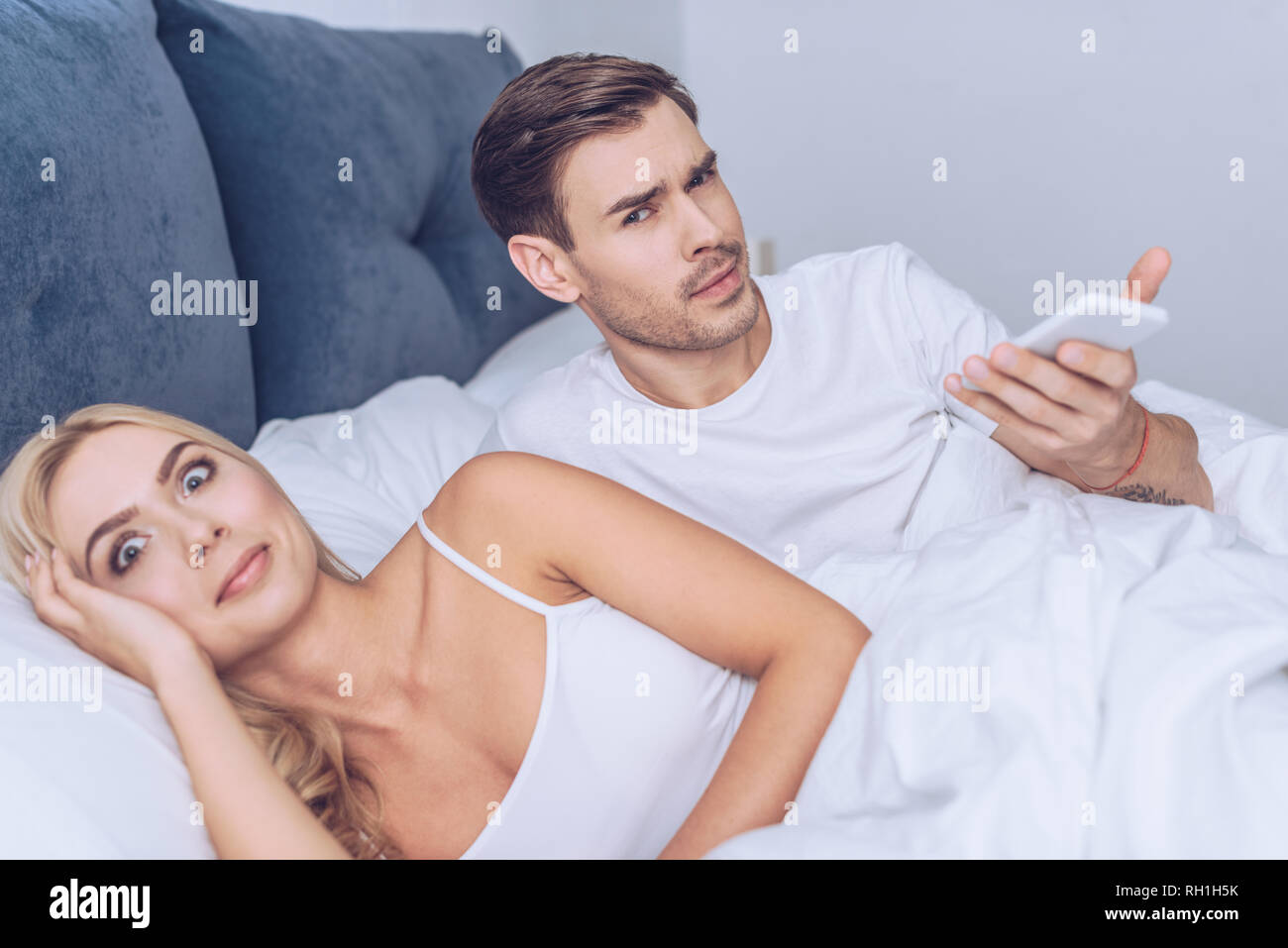 jealous young man holding smartphone and looking at camera while lying ...