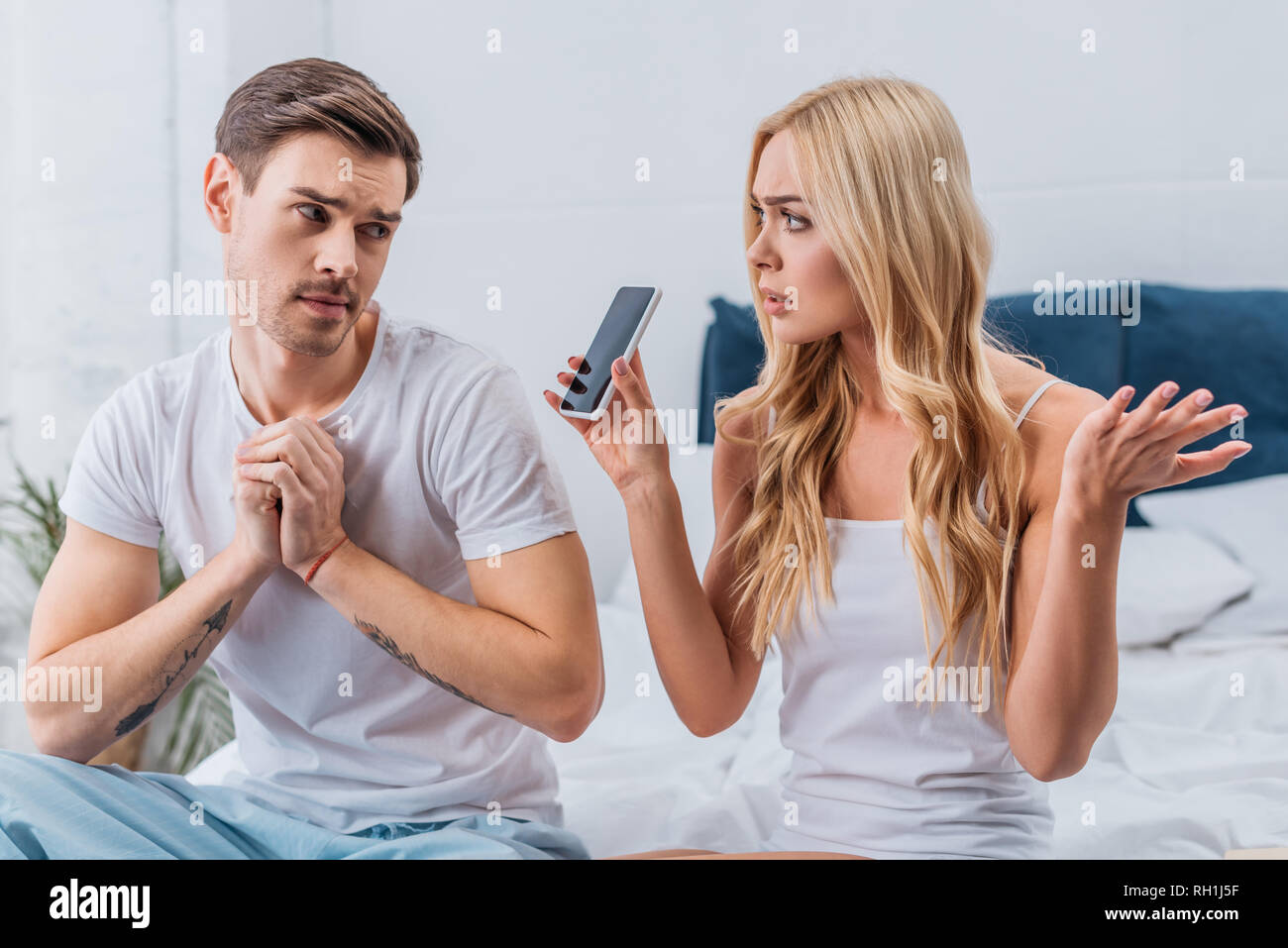 confused woman showing smartphone to suspicious boyfriend in bedroom ...