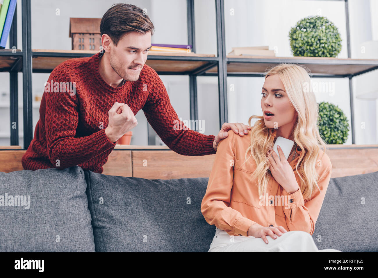 angry young man shaking fist and looking at scared girlfriend holding ...