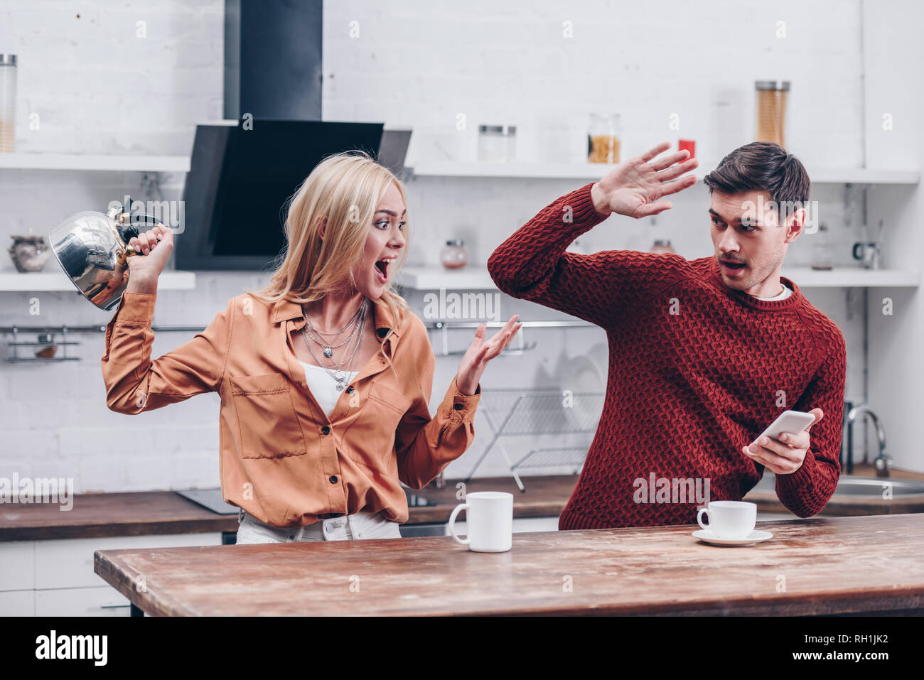 angry young woman with kettle yelling and husband with smartphone in ...