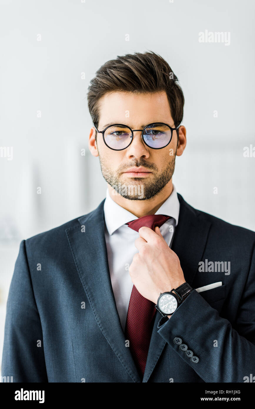 Handsome Businessman In Formal Wear And Glasses Adjusting Tie While