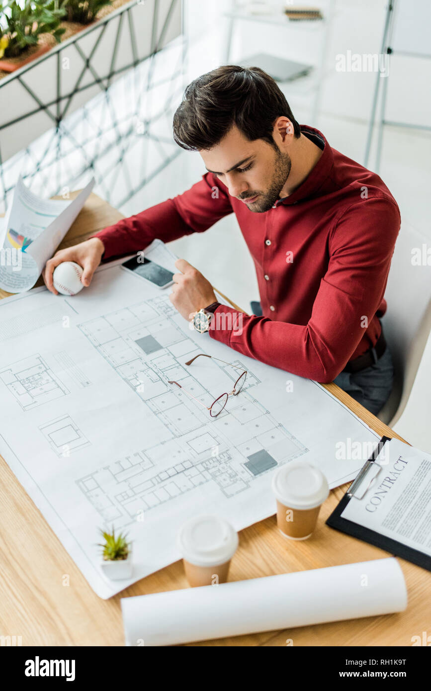 handsome male architect sitting and working on blueprint in office ...