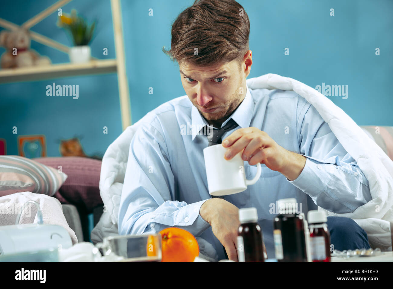 Bearded sick man with flue sitting on sofa at home covered with warm ...