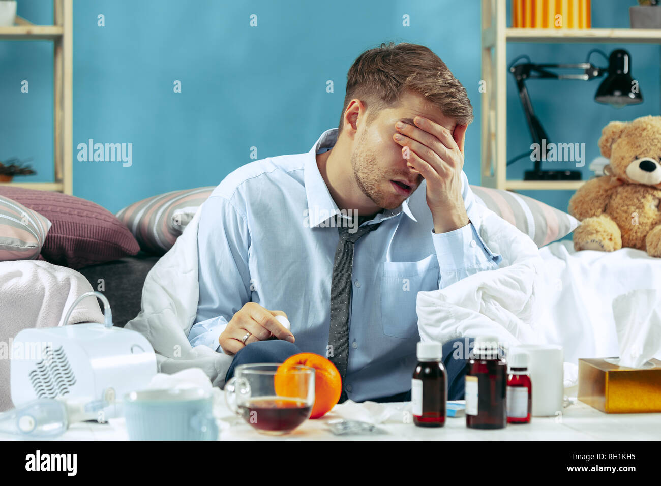 Bearded sick man with flue sitting on sofa at home covered with warm ...