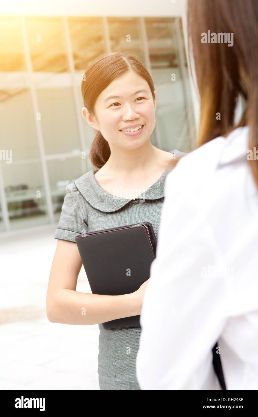 Asian businesswoman having conversation, office building as background ...