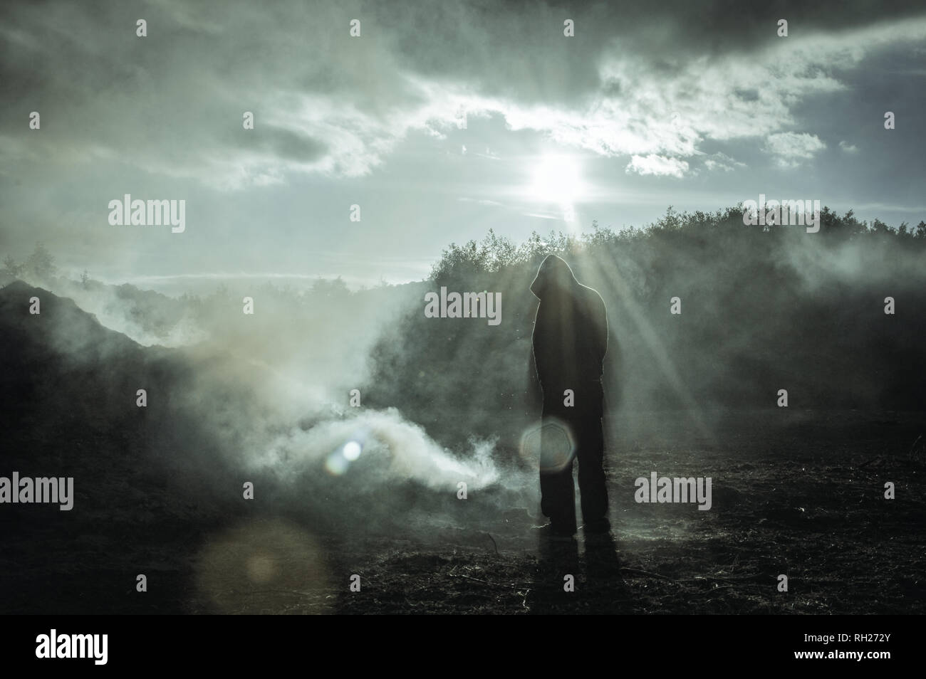 A lone hooded silhouetted figure standing outside. In a burnt smoking ...